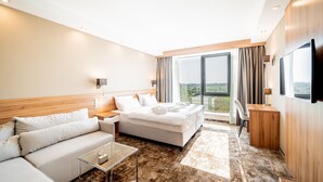 Quarto de hotel moderno com uma cama grande, um sofá, uma mesa pequena e uma televisão.