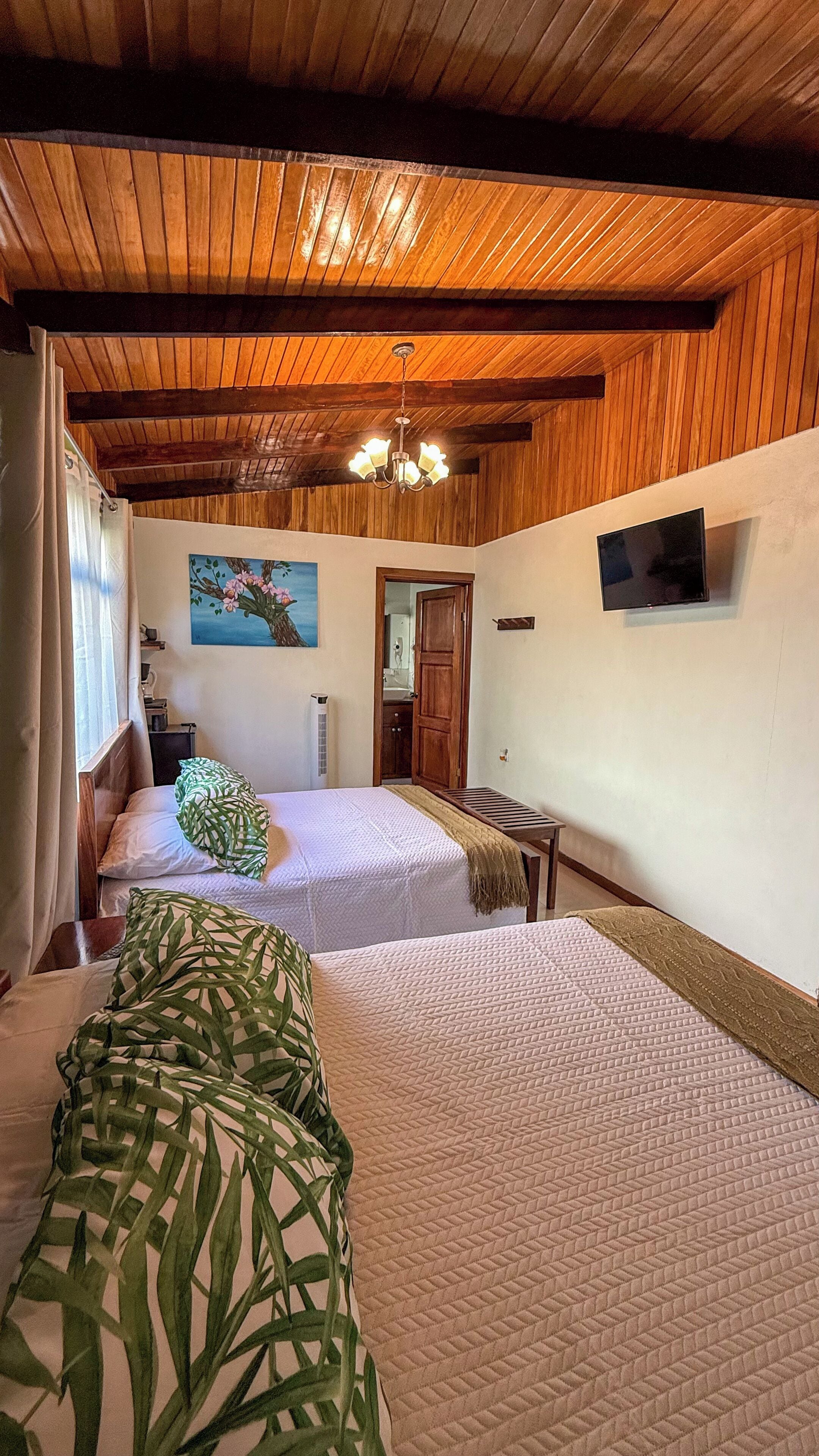 Quarto com duas camas, vigas de madeira no teto, um quadro na parede e uma pequena mesa.