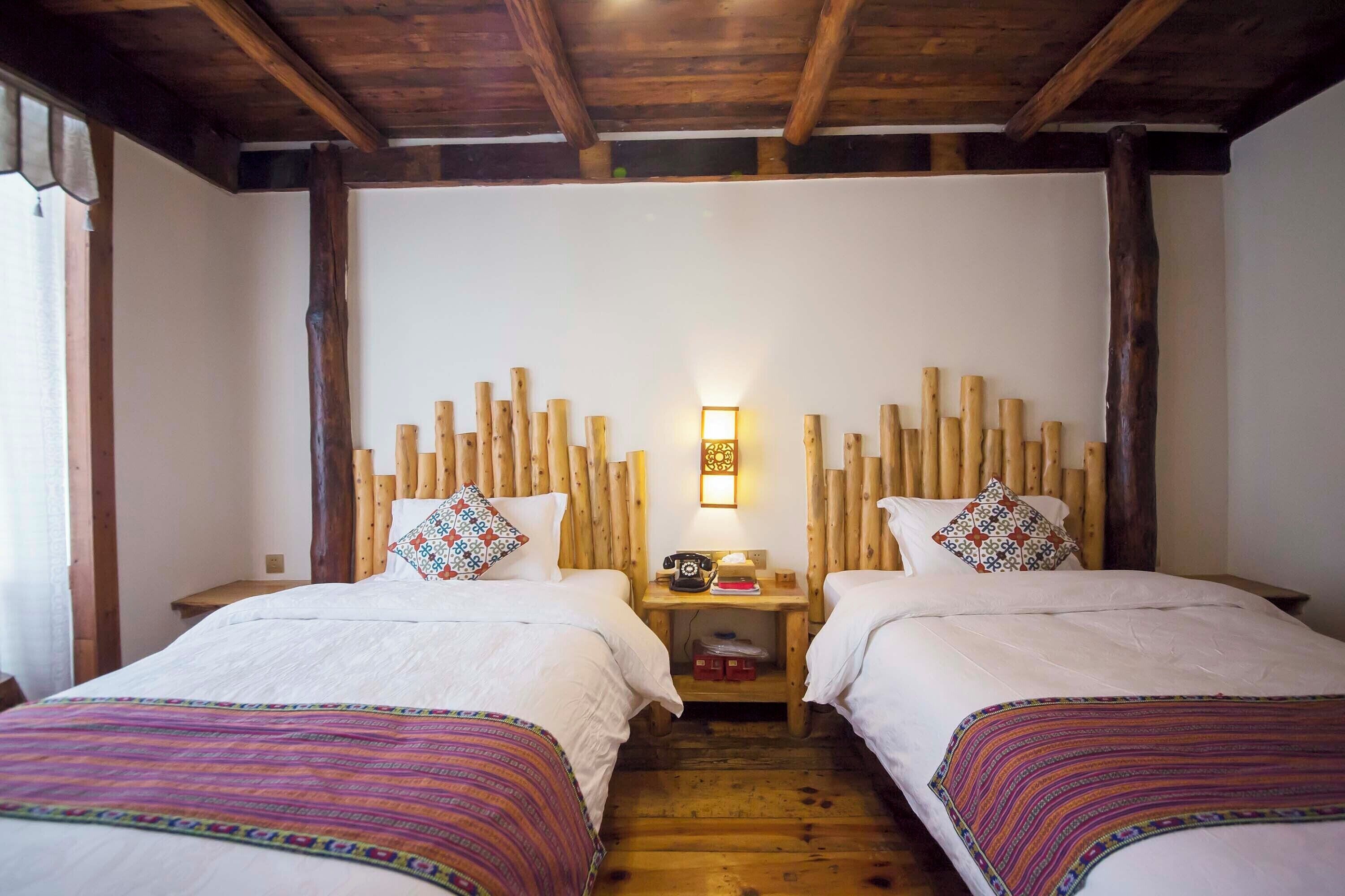 Quarto com duas camas, cabeceiras de madeira, mesa de cabeceira com luminária e manta decorativa.