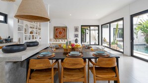 Uma área de refeições moderna com uma mesa grande, cadeiras de madeira e um lustre.