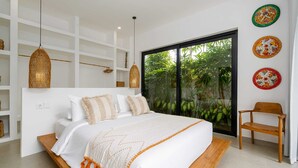 Quarto moderno com cama grande, paredes brancas e vista para o verde através de uma porta deslizante.