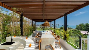 Terraço ao ar livre com uma mesa de jantar comprida, cadeiras e um espaço bar.