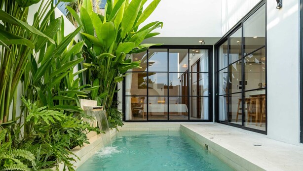 Piscina interna com parede de vidro, rodeada por plantas verdes exuberantes.