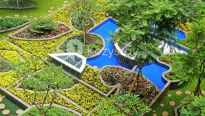 Um jardim paisagístico com uma piscina azul central, rodeado por canteiros variados e caminhos.