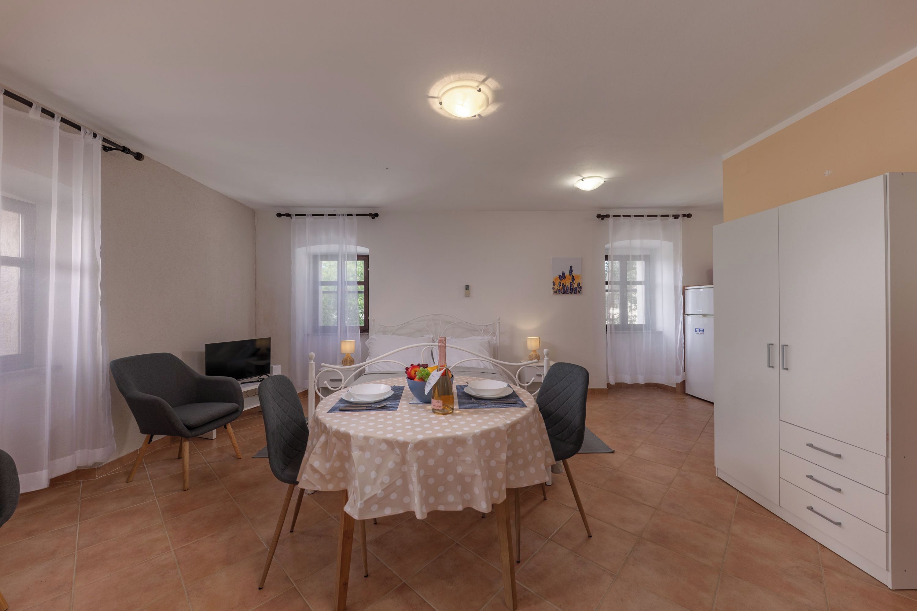Uma sala de jantar com uma mesa redonda, cadeiras, uma televisão e um armário.