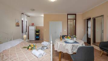 Quarto de hotel com cama, mesa de jantar com cadeiras, pequeno espaço de cozinha e um espelho.