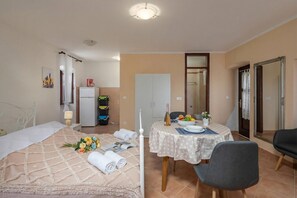 Quarto de hotel com cama, mesa de jantar com cadeiras, pequeno espaço de cozinha e um espelho.