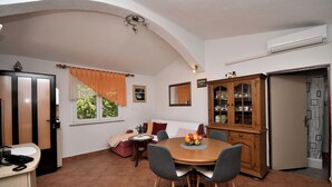 Uma sala de jantar com uma mesa redonda, cadeiras, um armário e uma janela com cortinas.
