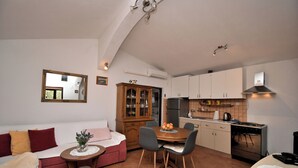 Um espaço compacto com cozinha compacta, área de refeições com mesa e cadeiras, sofá com almofadas e uma pequena mesa lateral com uma planta.
