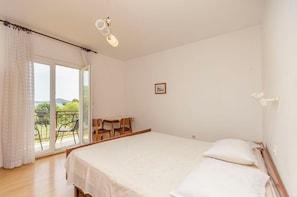 Quarto com cama, uma mesinha e cadeiras perto de uma porta de vidro deslizante que dá para uma varanda.
