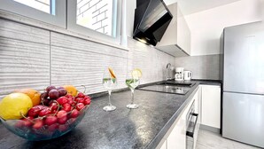 Uma cozinha moderna com bancada preta, uma tigela de frutas, duas taças de vinho, uma cafeteira e uma geladeira Bosch.
