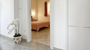 Quarto de hotel com cama, mesa de cabeceira, abajur e uma orquídea em vaso.