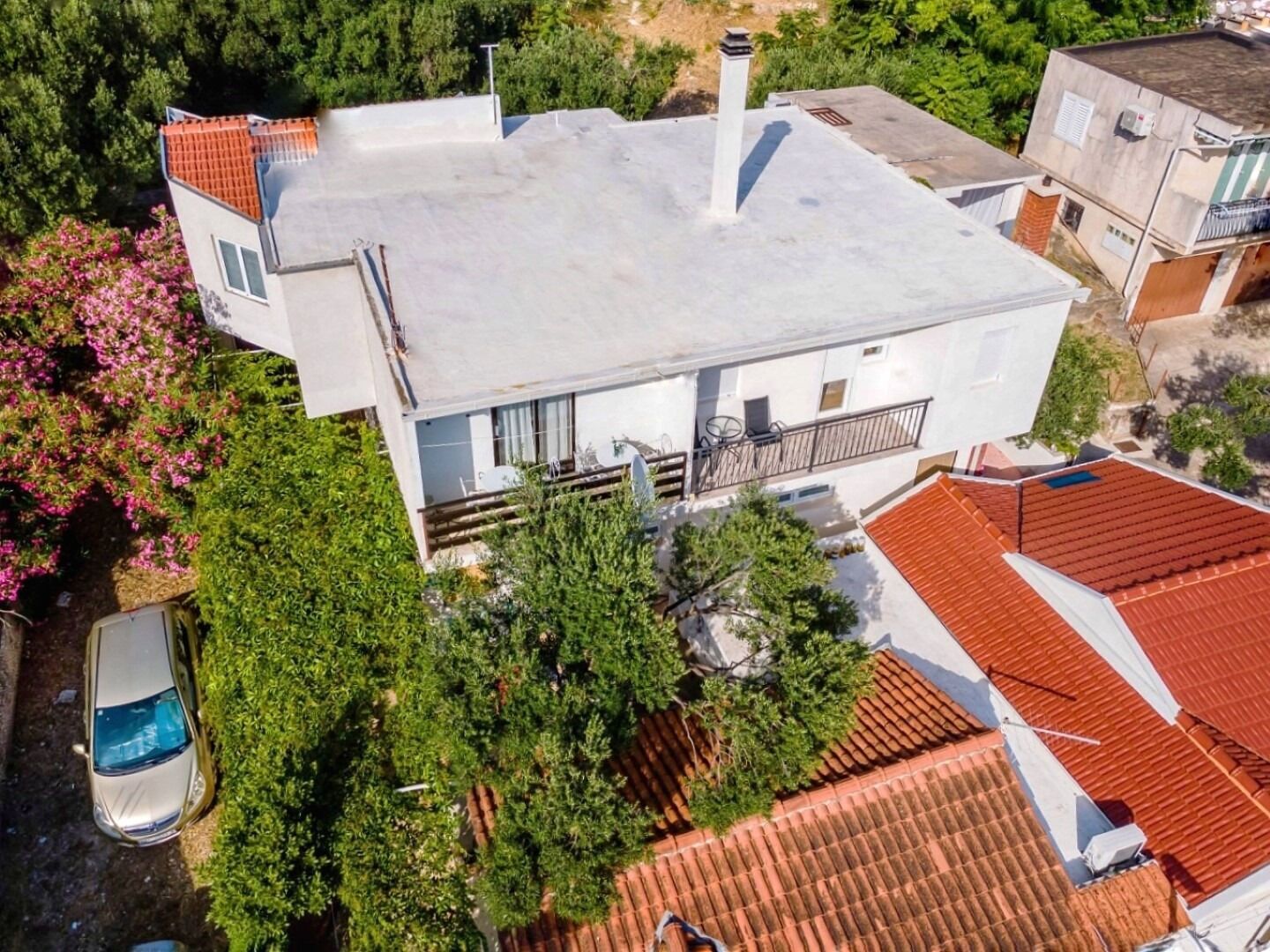 Uma casa branca de dois andares com teto plano, uma varanda e um carro estacionado na frente.