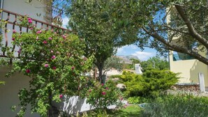 Um jardim com uma árvore florida em tons de rosa, uma piscina e um prédio com varanda.