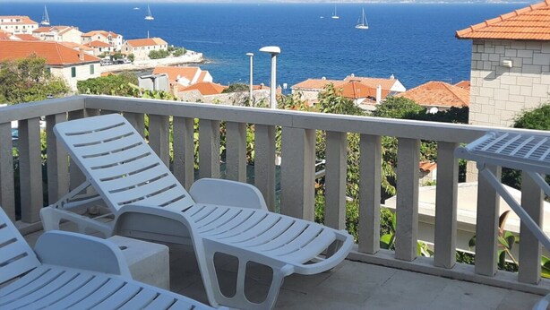 Varanda com cadeiras de plástico branco com vista para o litoral e veleiros.