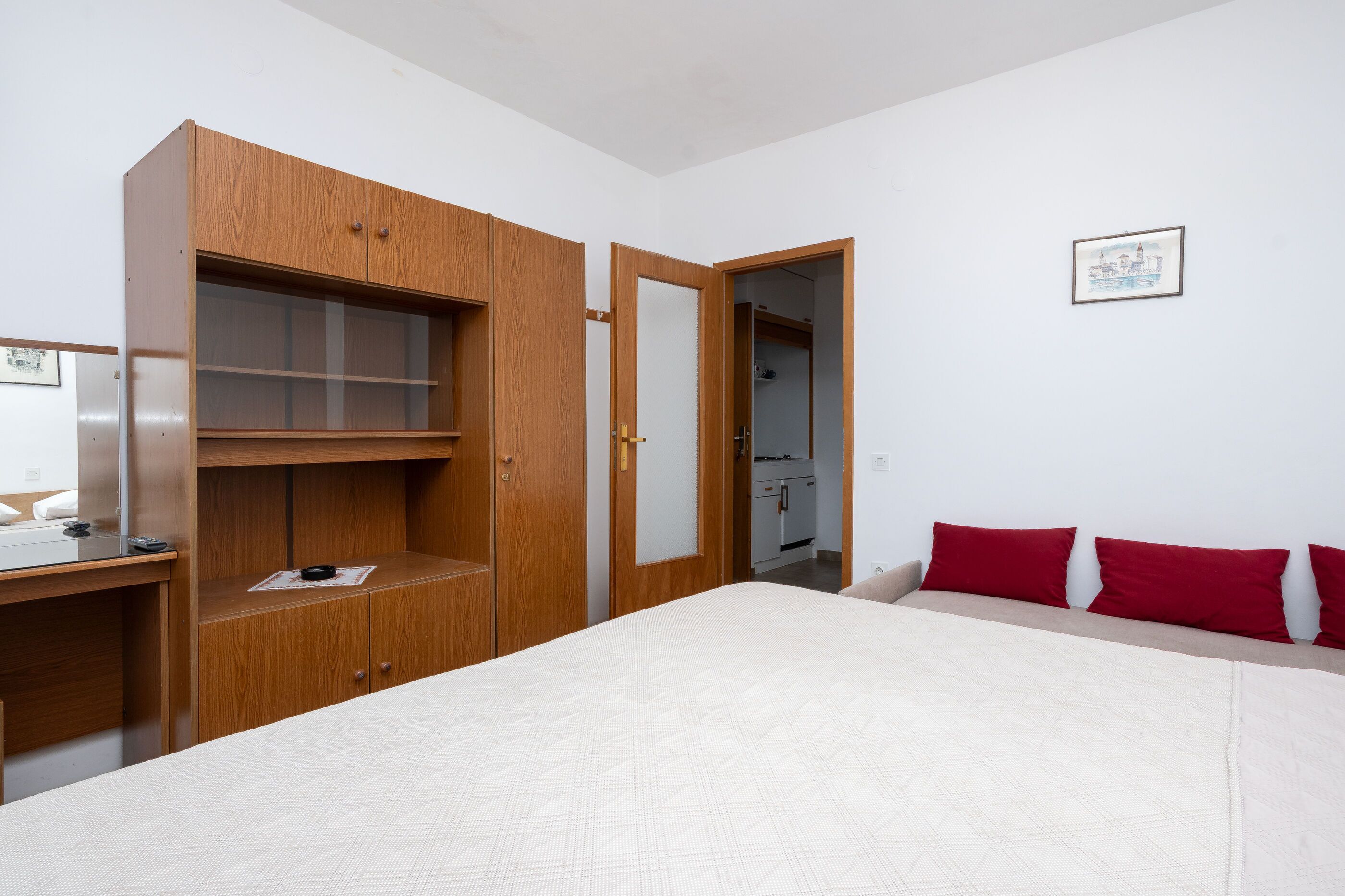 Um quarto com uma cama, um guarda-roupa de madeira, uma escrivaninha e um travesseiro vermelho.