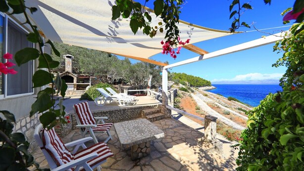 Um pátio com piso de pedra, cadeiras de lounge brancas e vista para o mar.