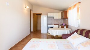 Quarto compacto com cama, uma mesinha com um vaso, cozinha compacta e porta que dá para outro cômodo.