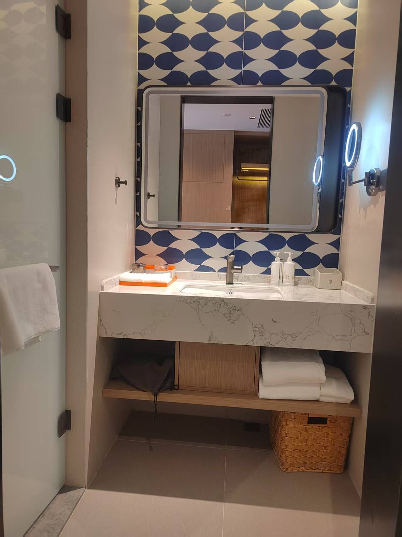 Casa de banho com lavatório de mármore branco, espelho com moldura retangular e parede com padrão.