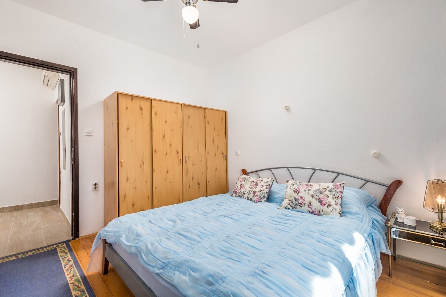 Quarto com cama, guarda-roupa, mesa de cabeceira e ventilador de teto.