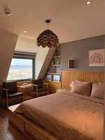 Quarto com uma cama grande, cabeceira de madeira, estante de livros e vista para a paisagem pela janela.
