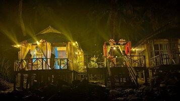 Uma estrutura de madeira rústica com entrada coberta e varanda, cercada por árvores e rochas.