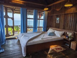 Quarto com cama, paredes de madeira e vista para o mar.