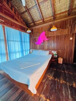Quarto de madeira com cama, mesa de cabeceira e um objeto rosa pendurado.