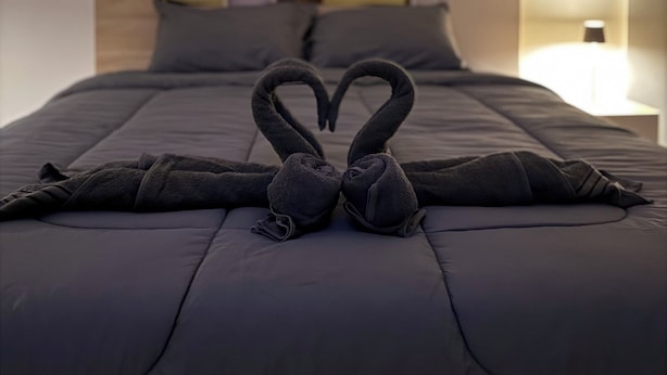 Uma cama com arranjo de toalhas em formato de coração e uma luminária de cabeceira.