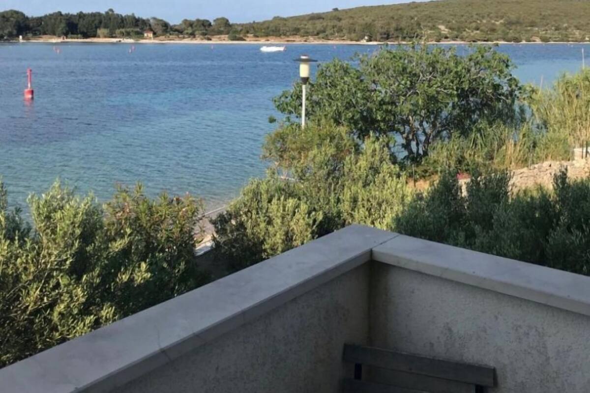 Uma varanda com vista para um mar tranquilo, uma linha de costa distante e alguma vegetação.