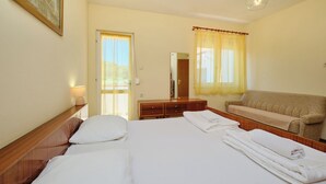 Quarto de hotel com cama, sofá, cómoda de madeira, espelho e janela com cortinas.