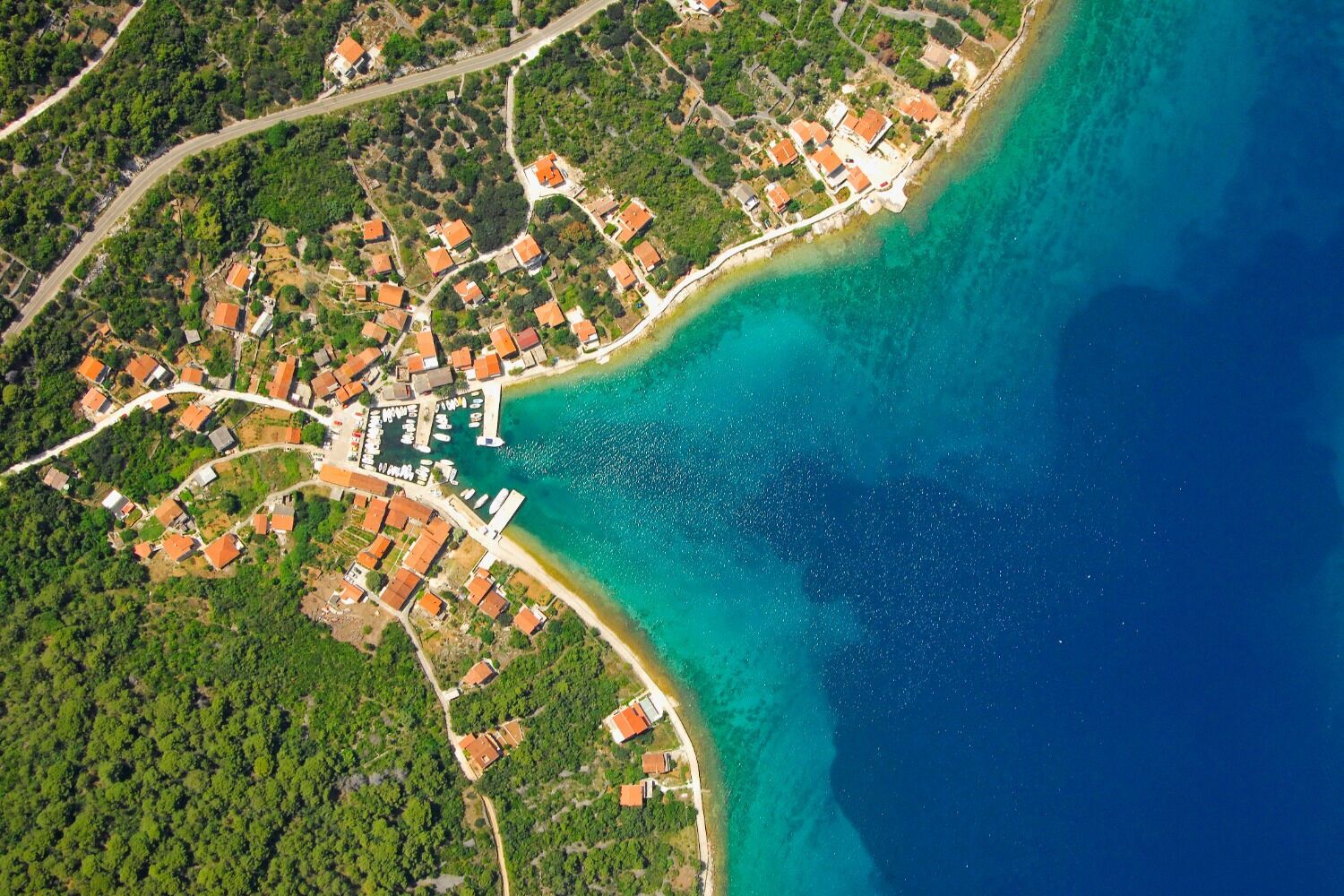 Vista aérea de uma cidade costeira com casas, um porto de iates e um mar azul cristalino.
