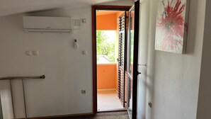 Um corredor com porta dando para uma varanda externa, corrimão e ar-condicionado fixado na parede.