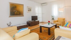 Uma sala de estar com sofá, mesa de centro, televisão e um quadro na parede.