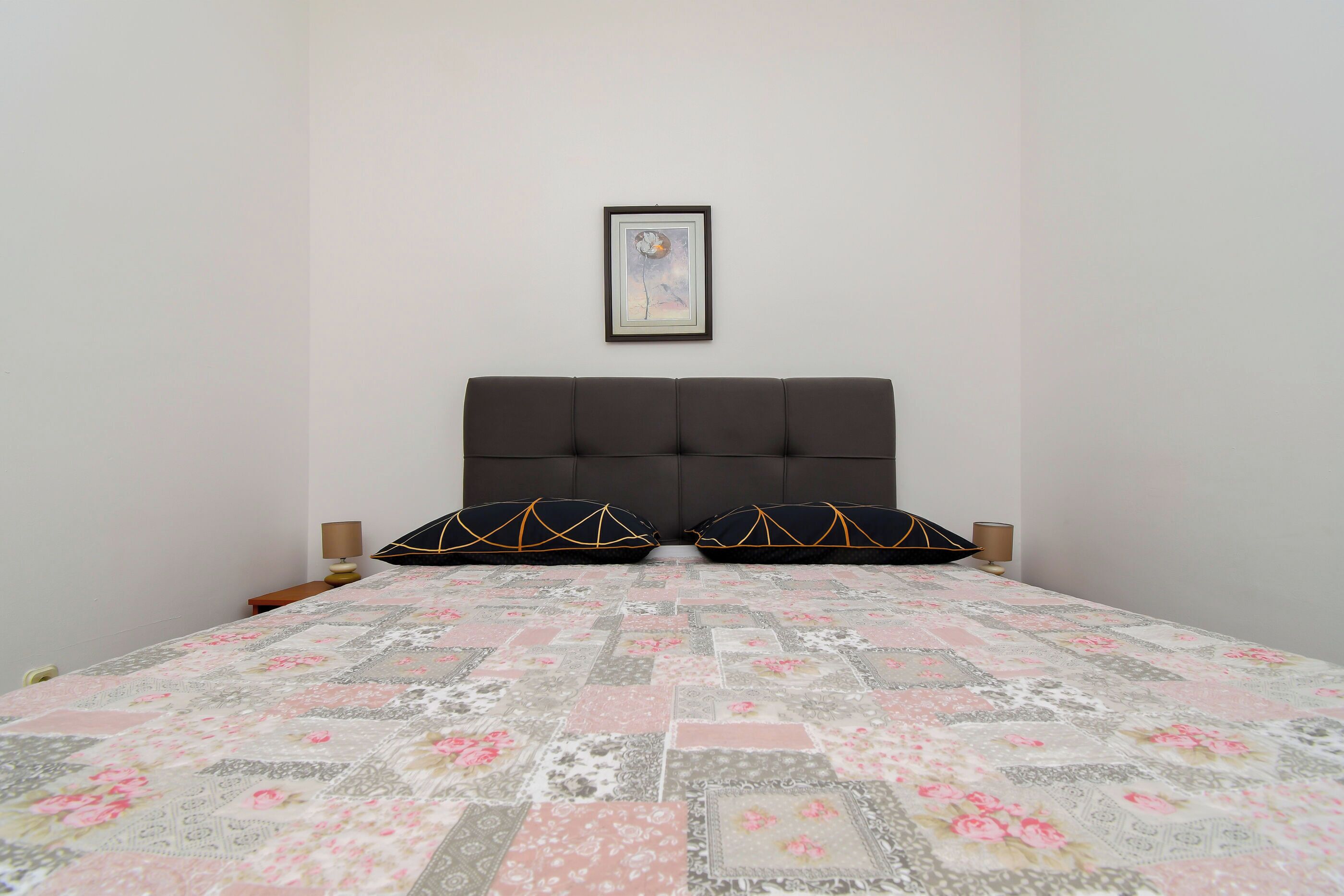 Quarto com cama, cabeceira, duas mesas de cabeceira e um quadro na parede.