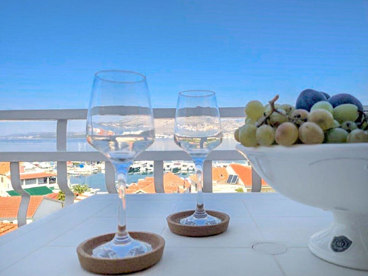 Mesa com duas taças de vinho e uma cesta de frutas, com vista para a costa.