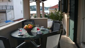 Varanda com mesa posta para dois, com uma tigela de frutas, duas xícaras e um copo.