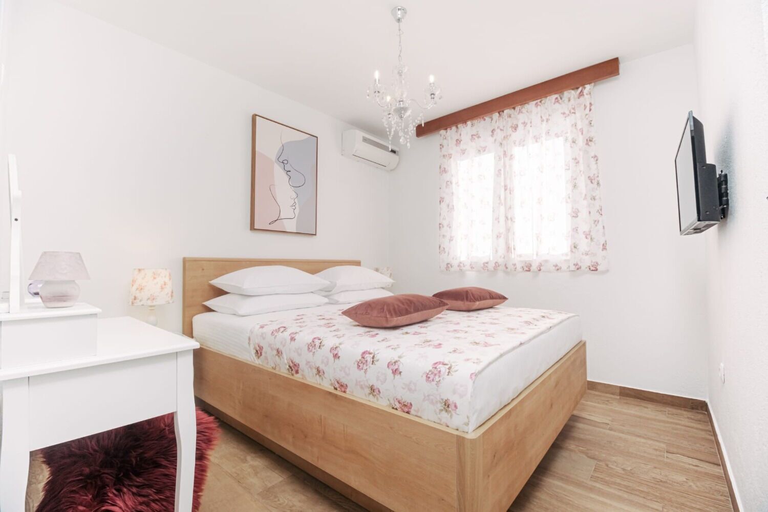 Quarto com cama de madeira, paredes brancas, um candelabro, televisão de tela plana e cortinas florais.