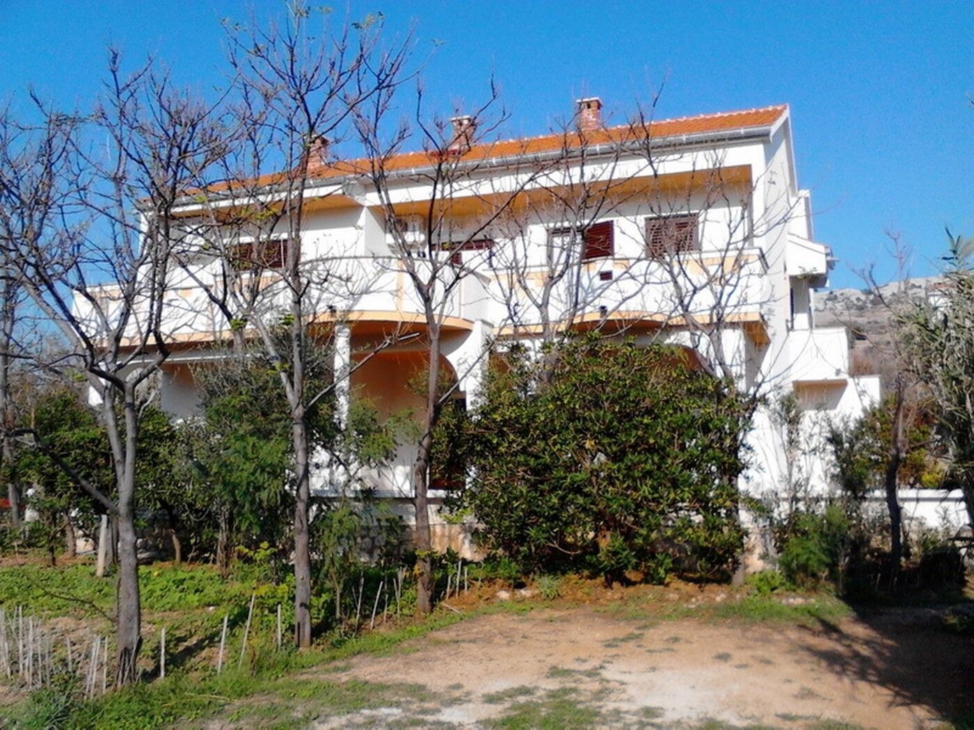Um edifício de dois andares com fachada branca e telhado em telhas laranja, rodeado por árvores e arbustos.
