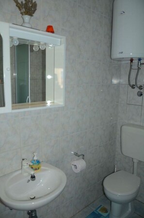 Casa de banho com lavatório branco, espelho, sanita e termoacumulador.