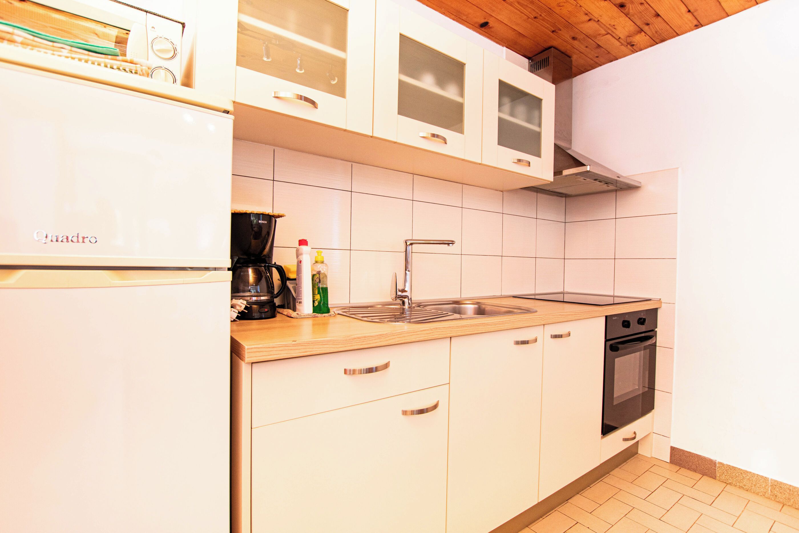 Cozinha com armários brancos, uma cafeteira Bosch, uma pia e um forno.