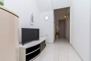 Um corredor com uma TV sobre um armário branco, um espelho em formato de coração na parede e uma escada que leva a outro quarto.