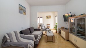 Uma sala de estar com sofá, mesa de centro, televisão e um armário com louças.