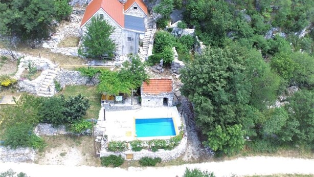 Uma casa de pedra com telhado vermelho, piscina e jardim.
