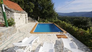 Piscina retangular com deck de pedra e cadeiras de descanso brancas.