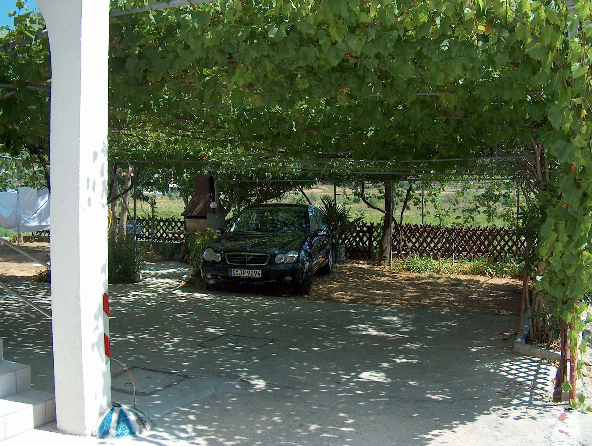Um carro estacionado sob uma pérgula com um pilar branco e um painel de treliça ao fundo.