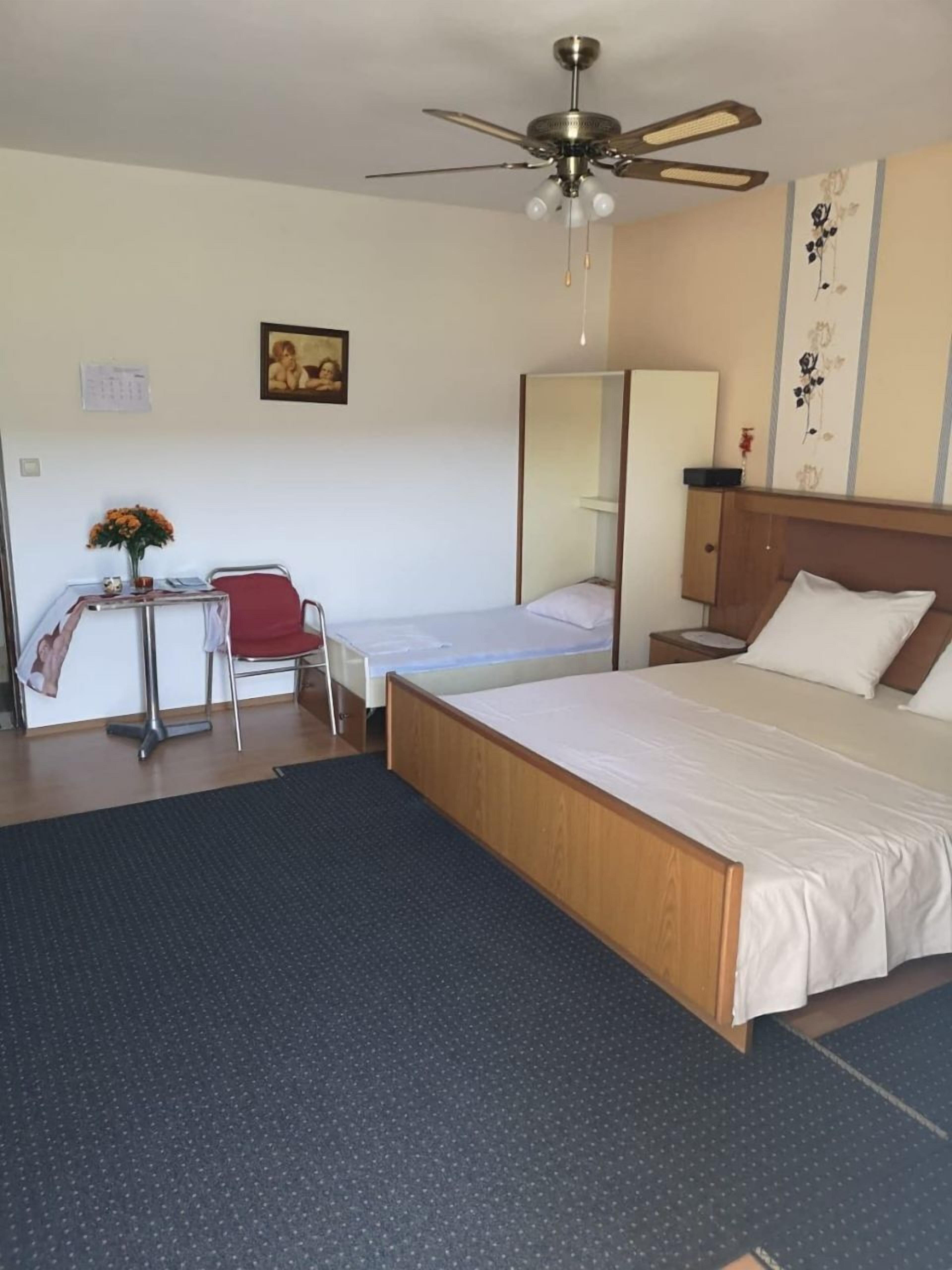 Quarto de hotel com uma cama grande, uma escrivaninha com cadeira, um ventilador de teto, um espelho e uma parede com desenho floral.
