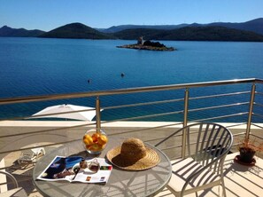 Varanda com mesa posta para refeição, com vista para um lago calmo com uma ilha pequena e montanhas ao longe.