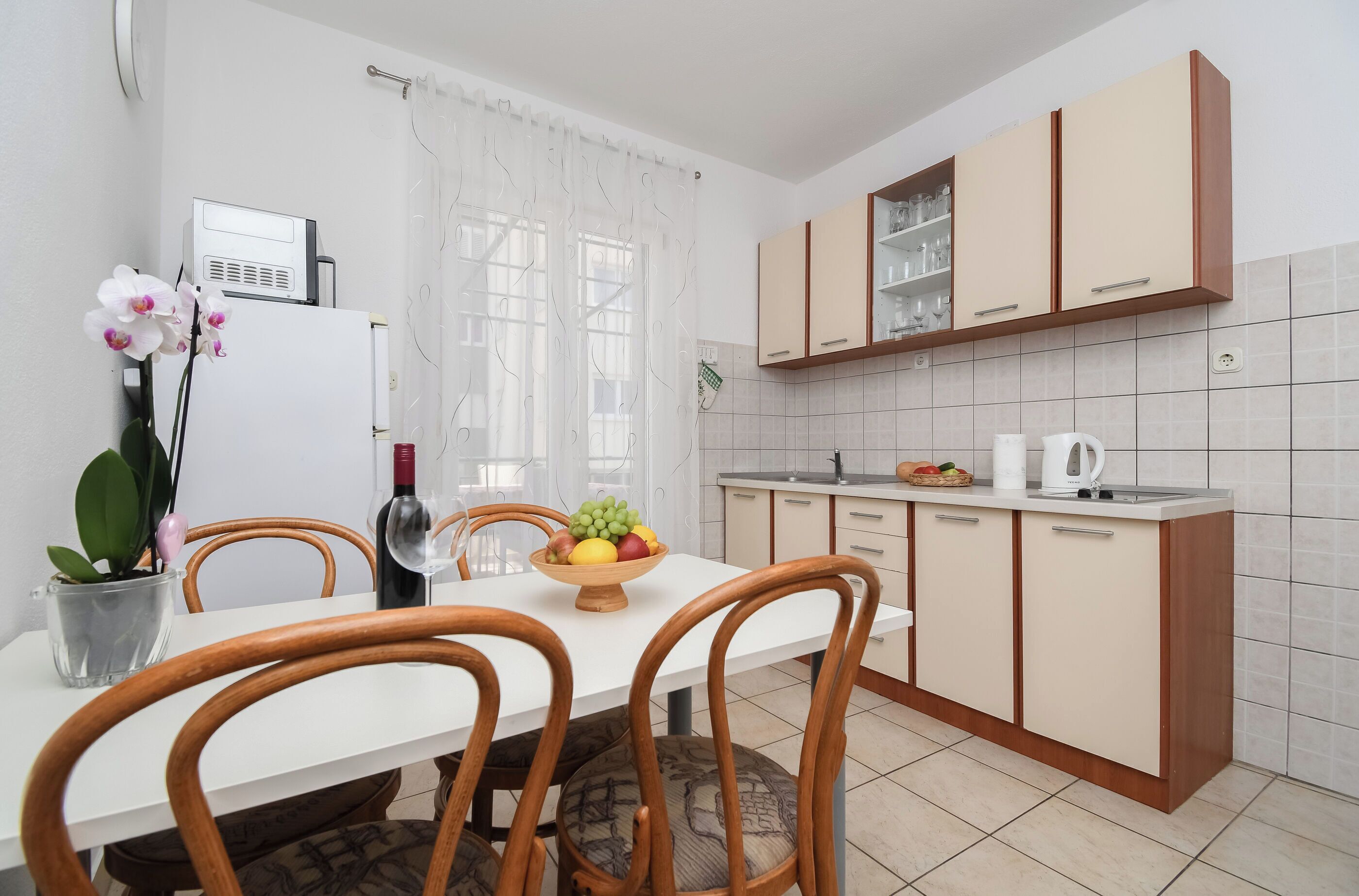 Uma cozinha com armários de madeira, bancada branca e mesa de jantar com cadeiras.
