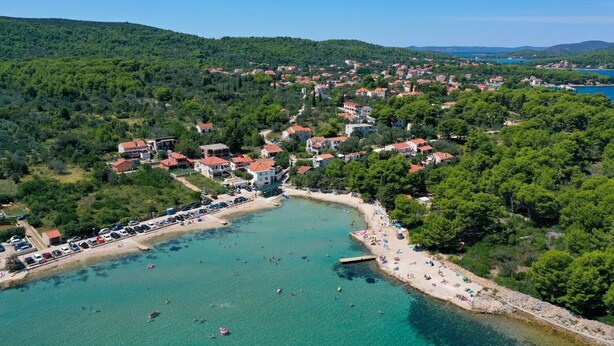 Vista aérea de uma cidade costeira com praia, águas turquesa cristalinas e vegetação ao redor.